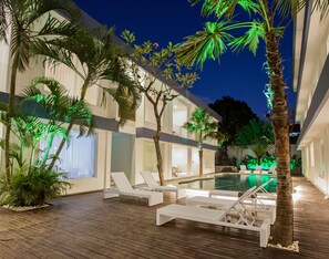 Uma área de piscina moderna ao ar livre, com espreguiçadeiras e palmeiras.