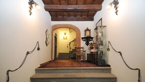 Uma escadaria com carpete estampado que leva a um quarto com um lustre, um relógio e um armário de vidro com garrafas.