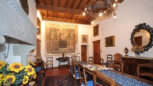 Uma sala de jantar com uma longa mesa de madeira, cadeiras estofadas azuis, um lustre e um quadro grande na parede.