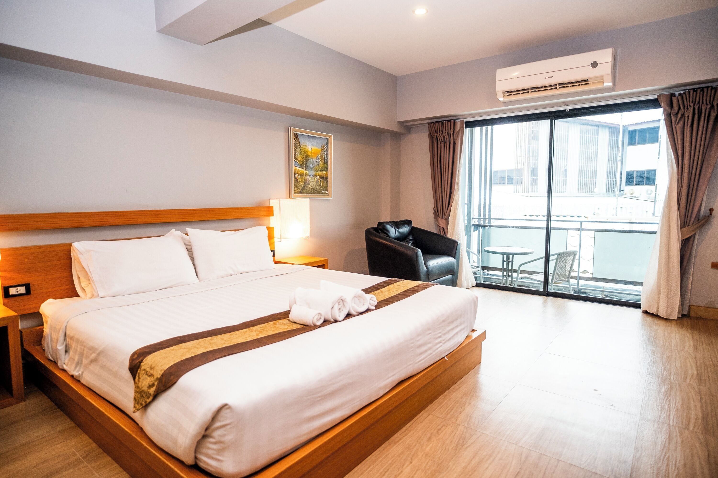 Quarto de hotel com uma cama grande, cabeceira de madeira, mesa de cabeceira, escrivaninha, cadeira, varanda com vista e ar condicionado.