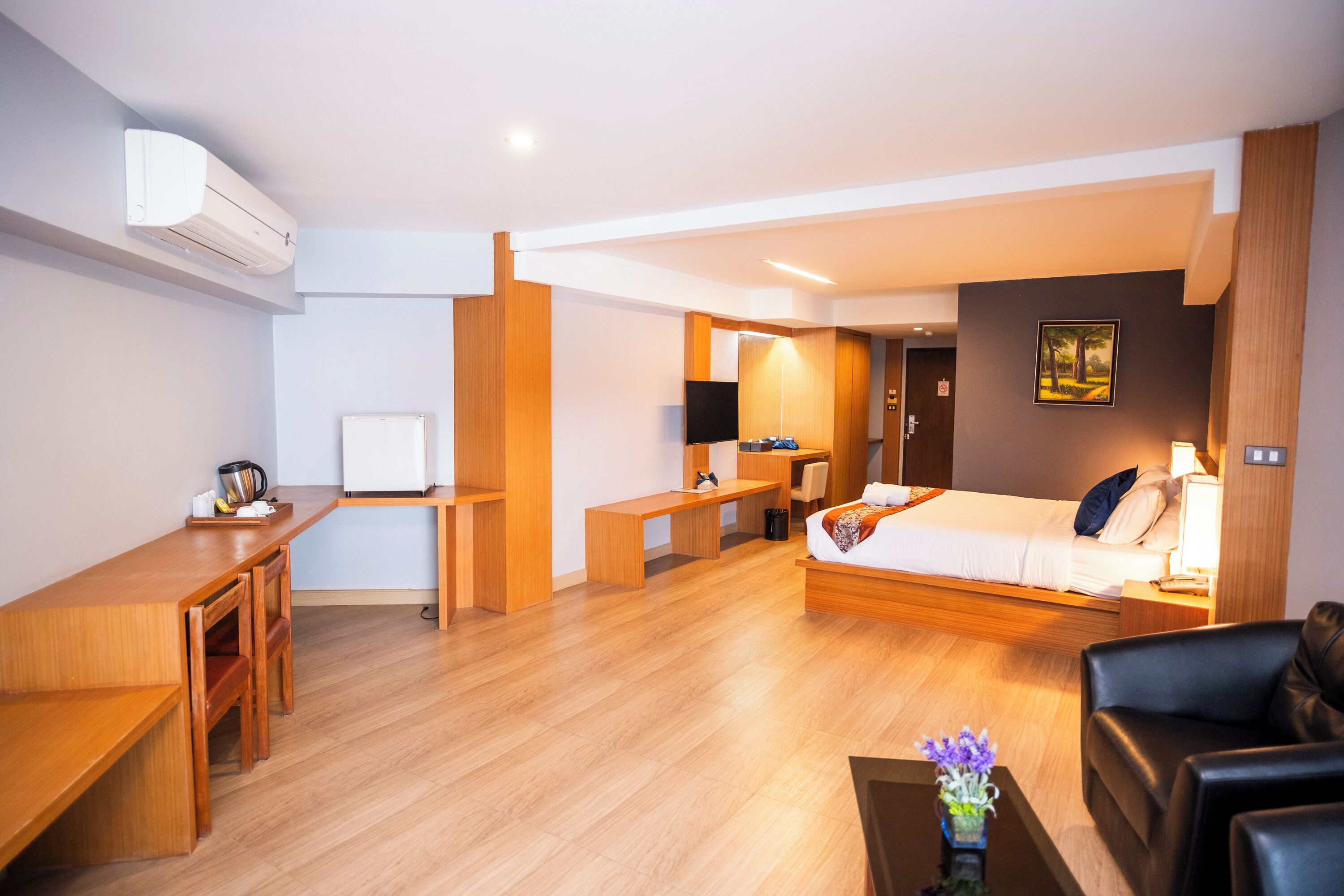 Quarto de hotel moderno com uma escrivaninha de madeira, cama, sofá, televisão e um quadro na parede.