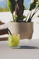 Um copo com bebida verde, canudo e uma fatia de laranja sobre toalha xadrez.
