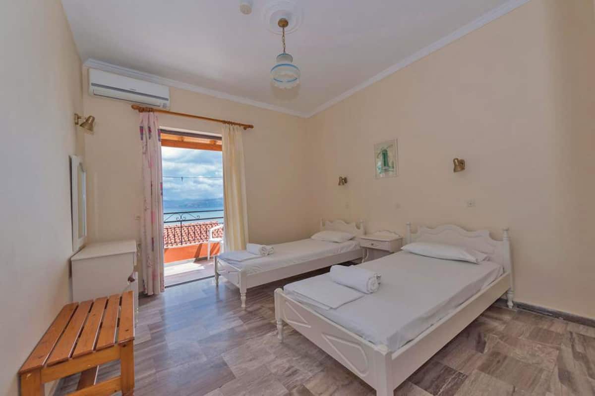 Quarto com duas camas de solteiro, um banco de madeira, ar condicionado e varanda com vista.