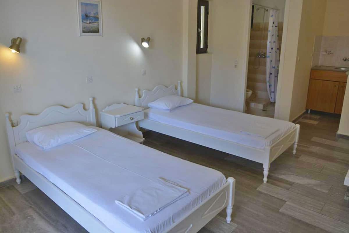Quarto com duas camas de solteiro, uma mesinha e banheiro visível através de uma porta aberta.