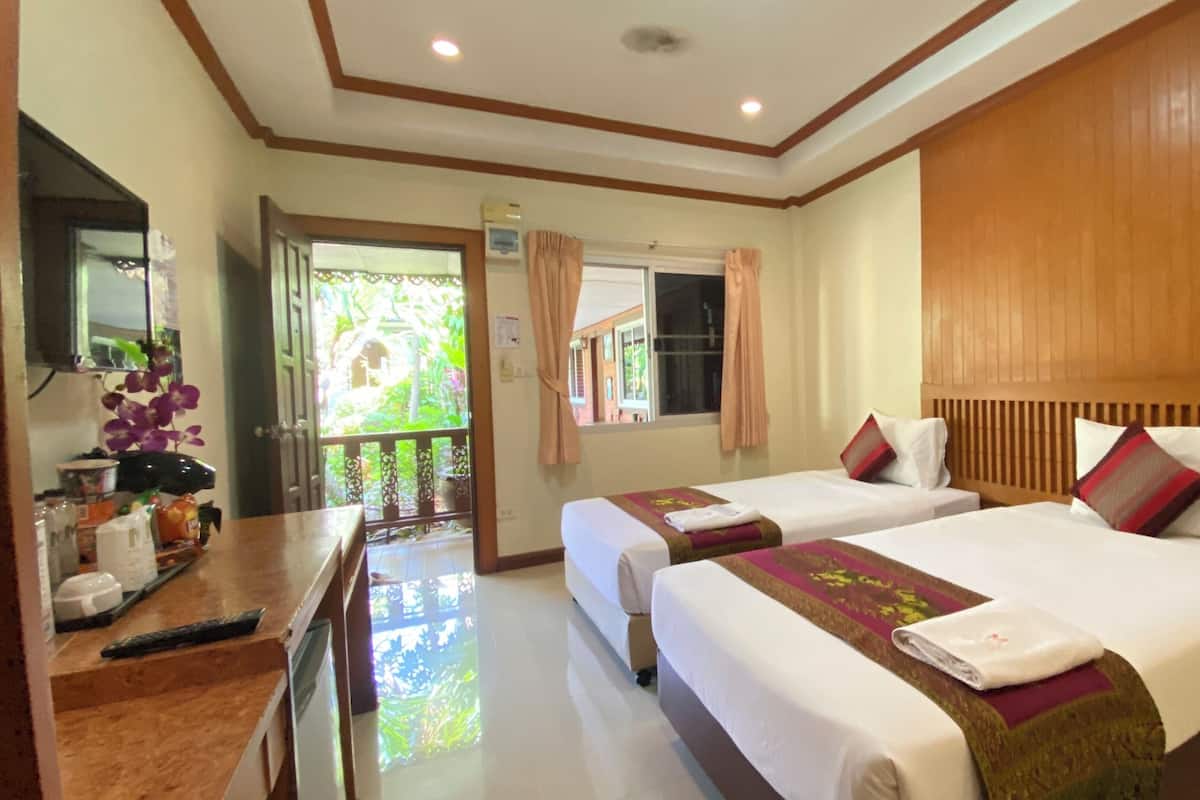 Quarto de hotel com duas camas, cabeceira de madeira, escrivaninha com computador e vista para o verde lá fora.