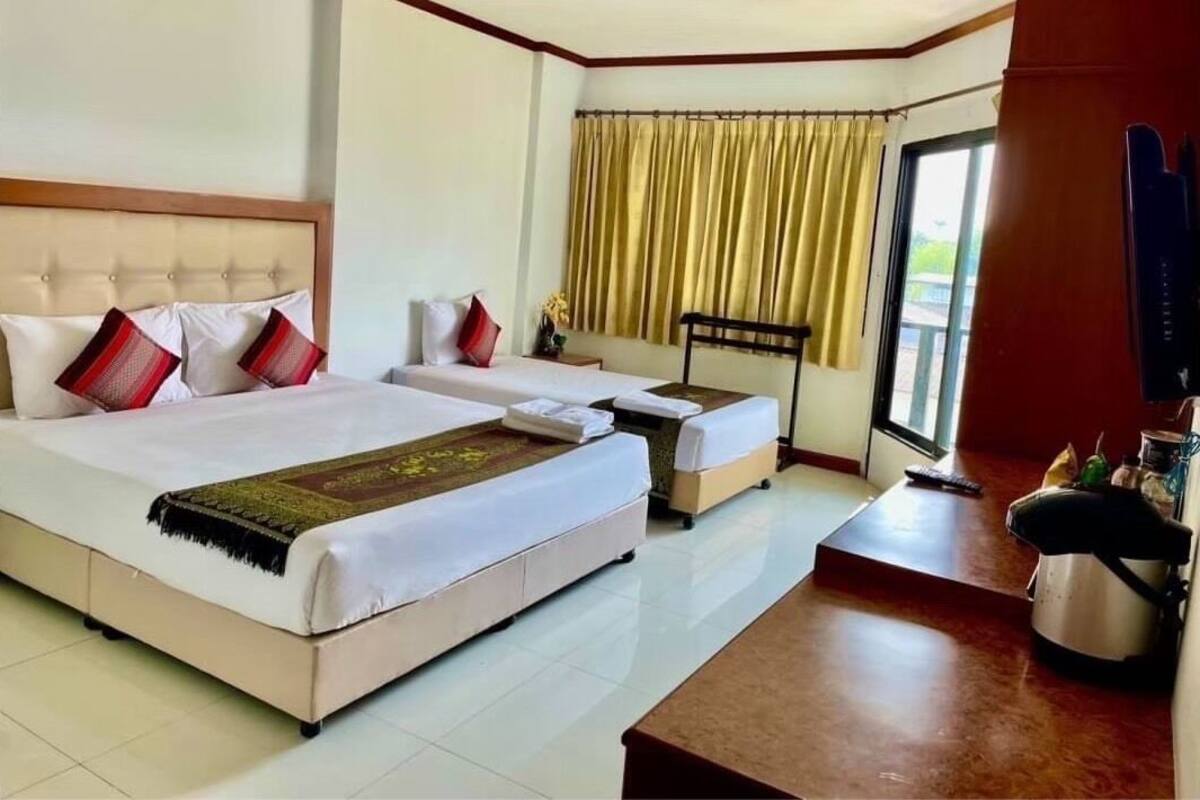 Quarto de hotel com duas camas, um sofá, uma escrivaninha, uma televisão e uma janela com cortinas.