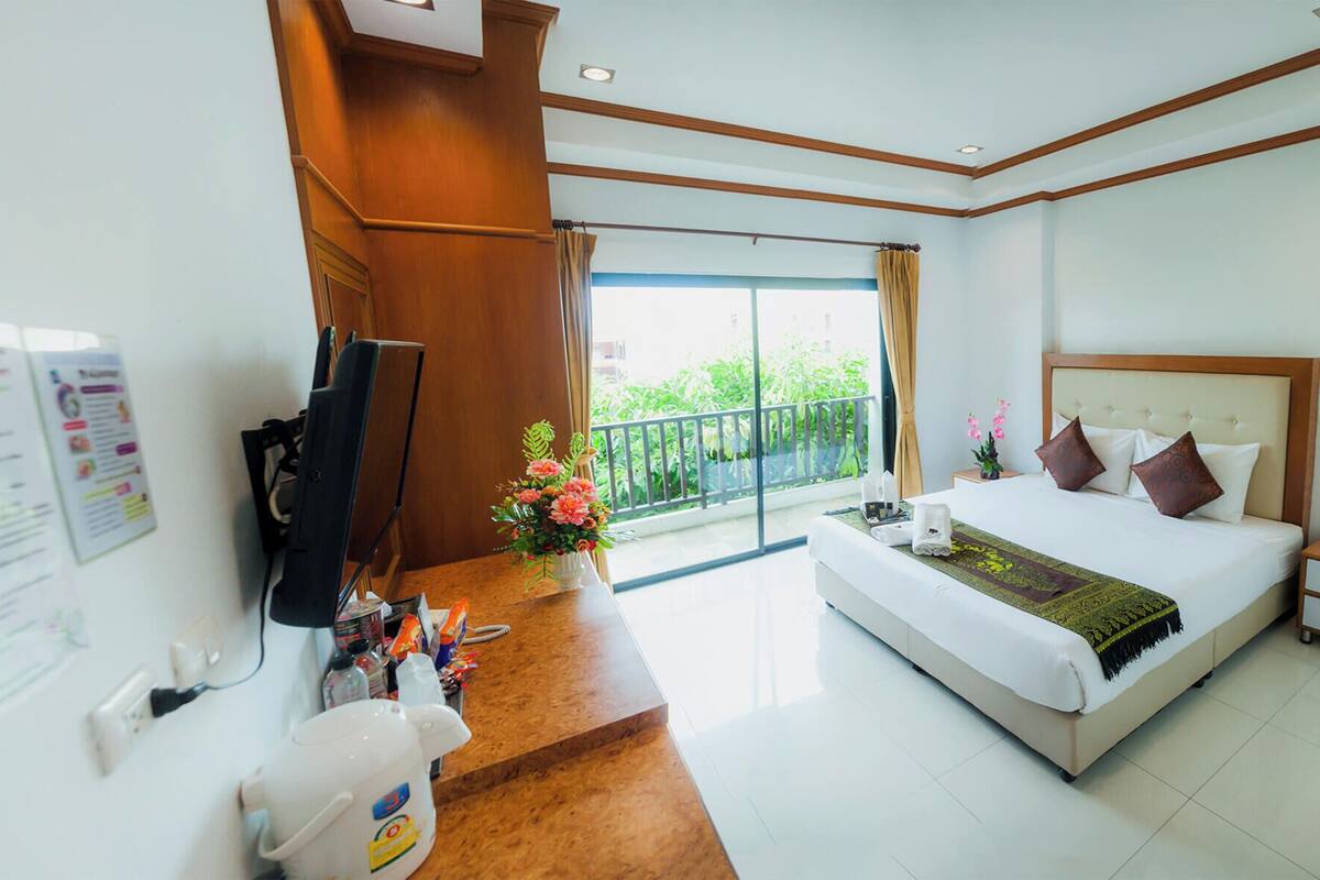 Quarto de hotel com cama, televisão, escrivaninha com cafeteira e varanda com plantas.