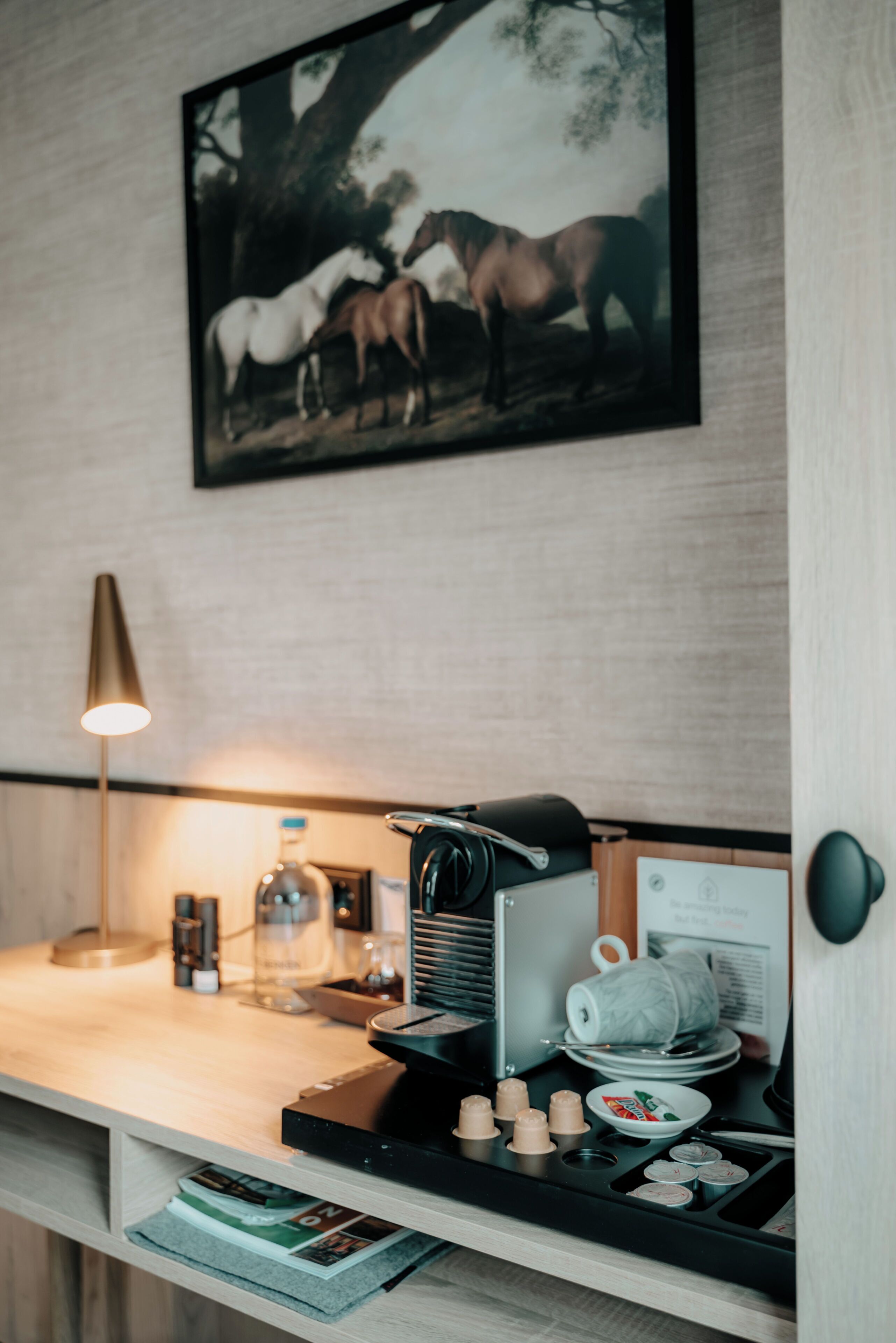 Uma cozinha compacta com cafeteira, chá e uma moldura com uma imagem de cavalos na parede.