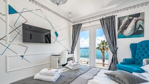 Quarto de hotel moderno com cama, escrivaninha, televisão e vista para o mar.