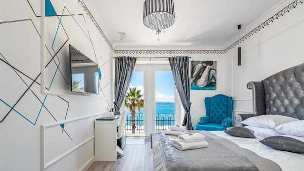 Quarto moderno com uma cama grande, uma poltrona azul e vista para o mar.