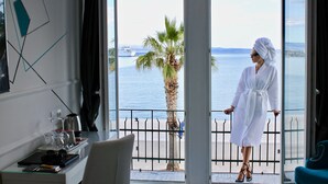 Quarto com varanda e vista para a água, uma palmeira e um cruzeiro.