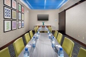 Uma sala de conferências com uma mesa comprida, cadeiras, garrafas de água e quadros nas paredes.