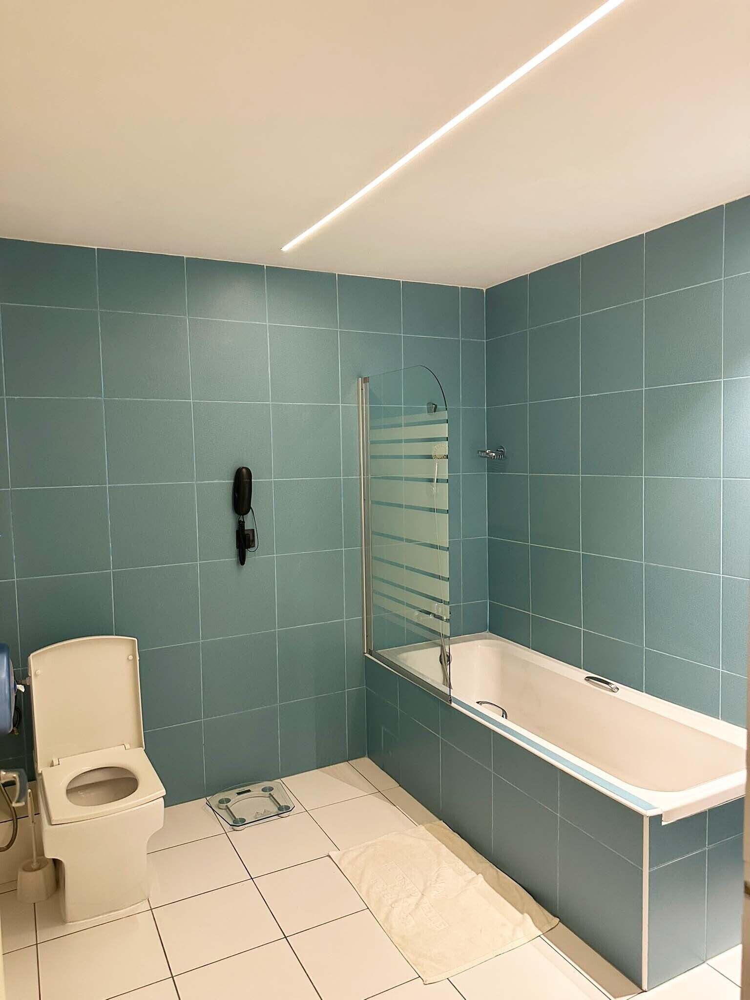 Casa de banho com azulejos verde-água, sanita branca, cabine de duche em vidro e banheira branca.
