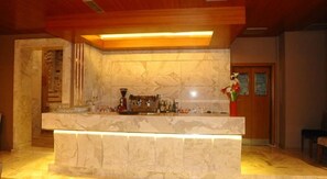 Uma área de bar com bancada de mármore, uma máquina de café e um vaso com flores.