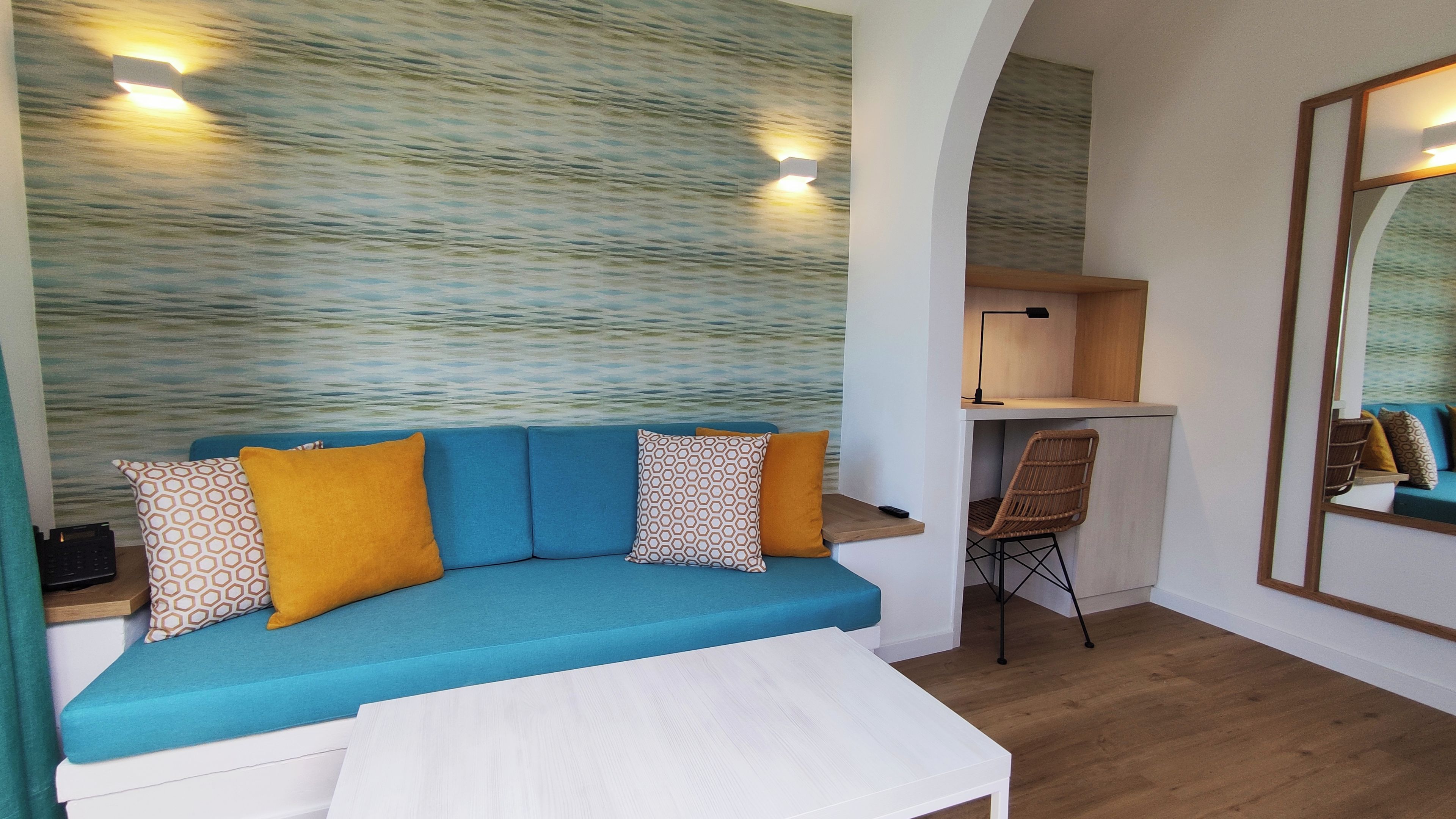 Uma sala de estar moderna com um sofá azul, almofadas estampadas, uma mesa de centro branca e piso de madeira.