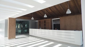 Uma área de recepção moderna com teto de madeira, iluminação pendente e balcão de recepção branco.