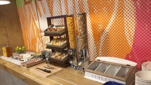 Disposição de buffet com diversos alimentos, um espaço para leite e uma área com talheres.
