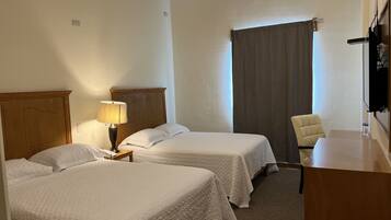Quarto de hotel com duas camas, uma escrivaninha, uma cadeira, uma luminária e uma televisão.