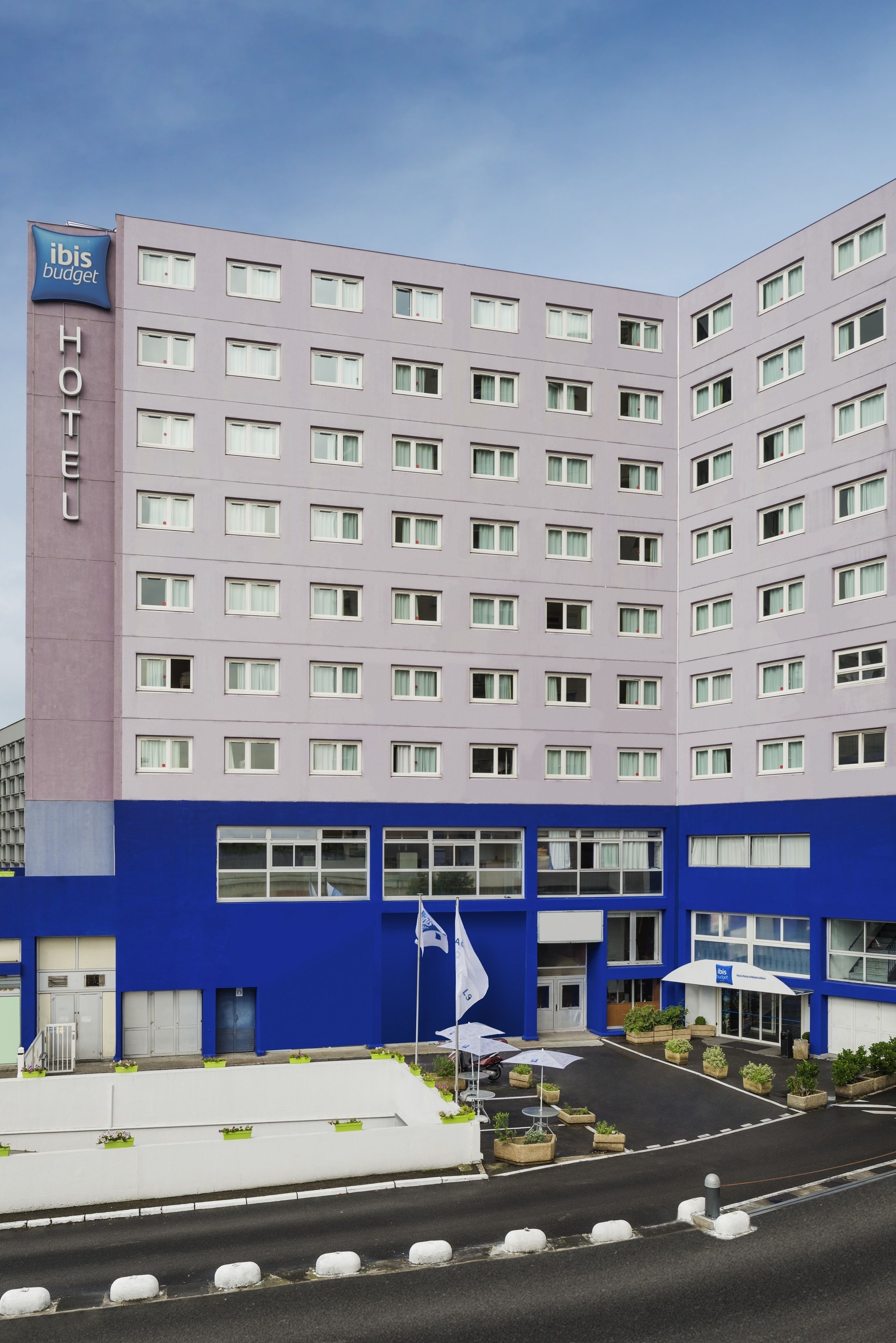 Um hotel com design moderno, com um destaque para a placa 'HOTEL' na fachada, várias janelas e um esquema de cores azul e branco.