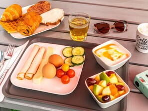 Bandeja de refeição com croissants, queijo, ovos, tomate, pepino e uma cesta de frutas.