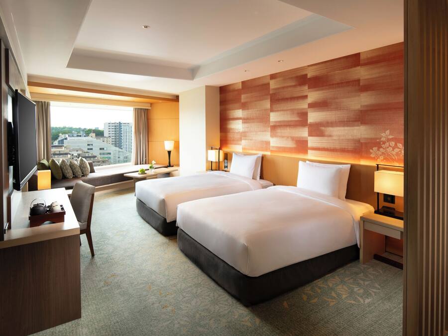 Quarto de hotel com duas camas, uma escrivaninha, uma televisão e vista para a cidade.