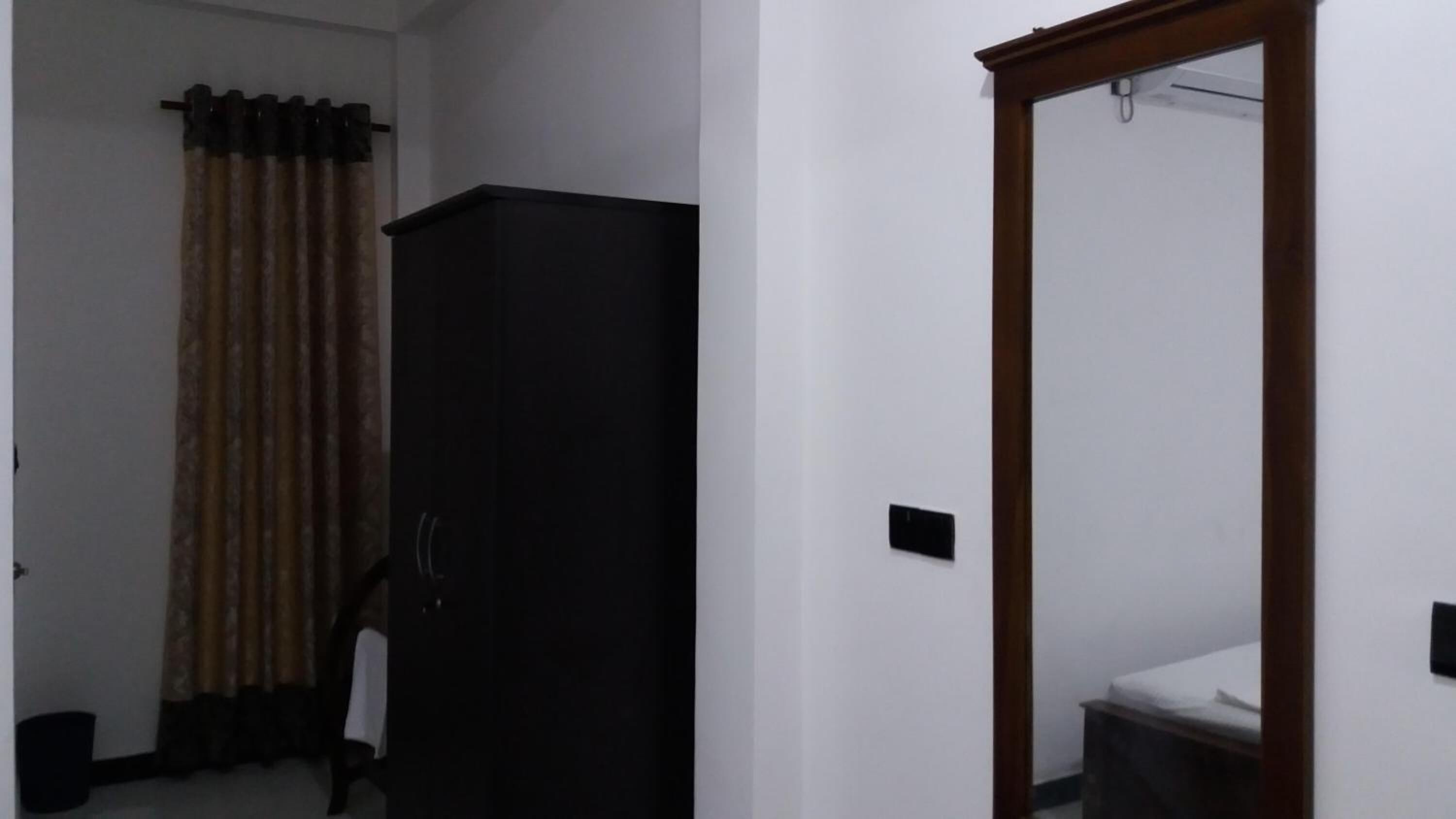Quarto com guarda-roupa preto, cortina, porta e uma pequena mesa de cabeceira.