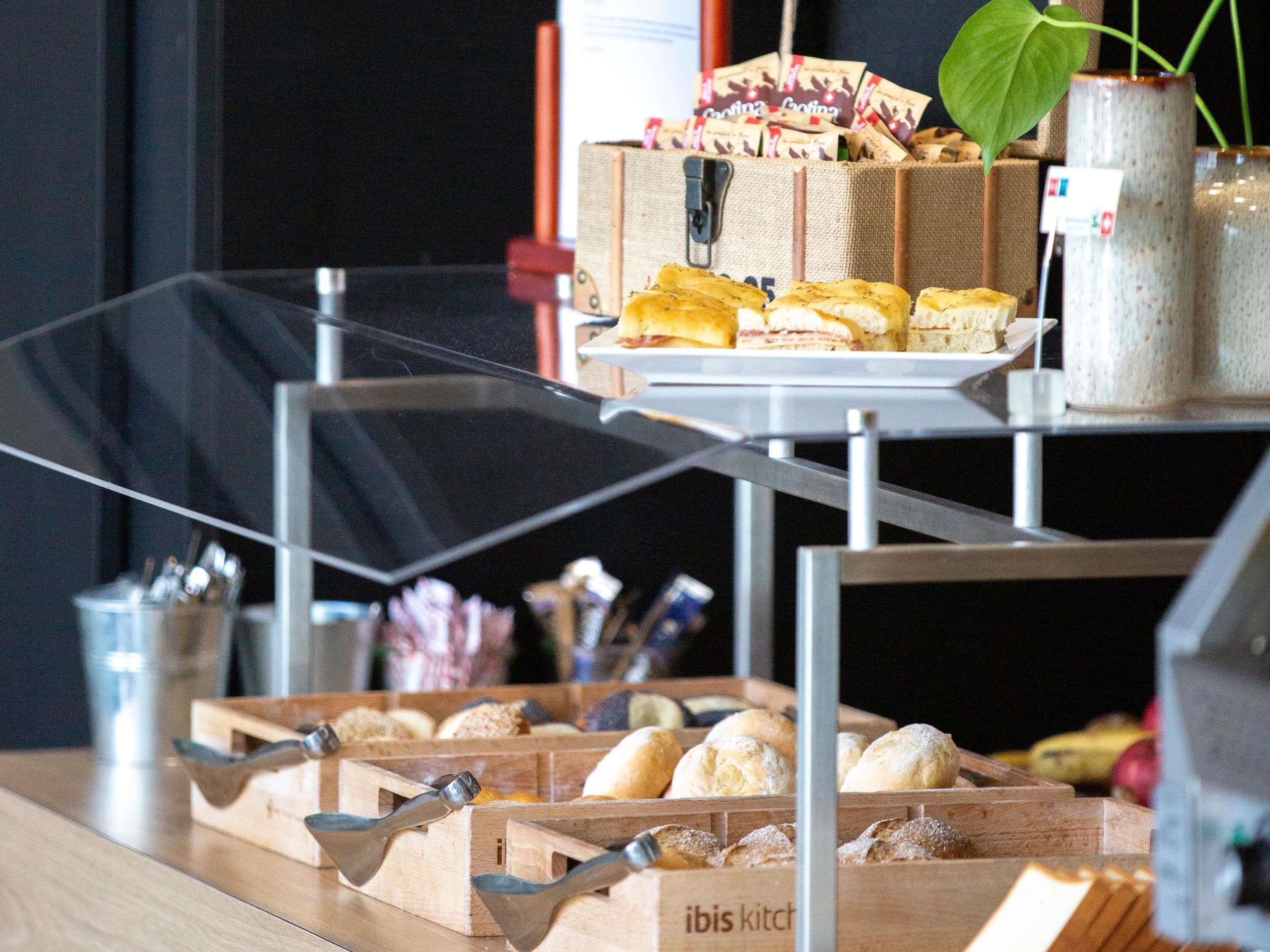 Disposição de buffet com diversos alimentos e uma planta ao fundo.