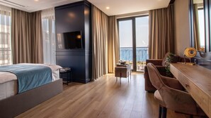 Quarto de hotel moderno com uma cama grande, uma escrivaninha, televisão e varanda com vista.