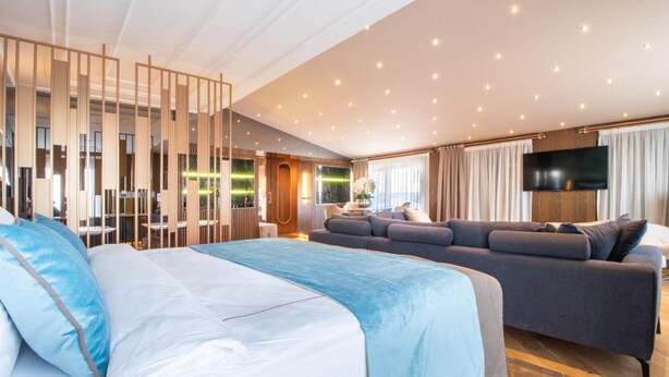 Quarto de hotel espaçoso com uma cama grande, um sofá, uma TV e um divisória decorativa.