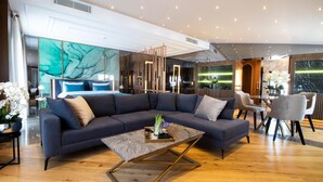 Uma sala de estar moderna com um sofá seccional azul escuro, uma mesa de centro de vidro e piso de madeira.
