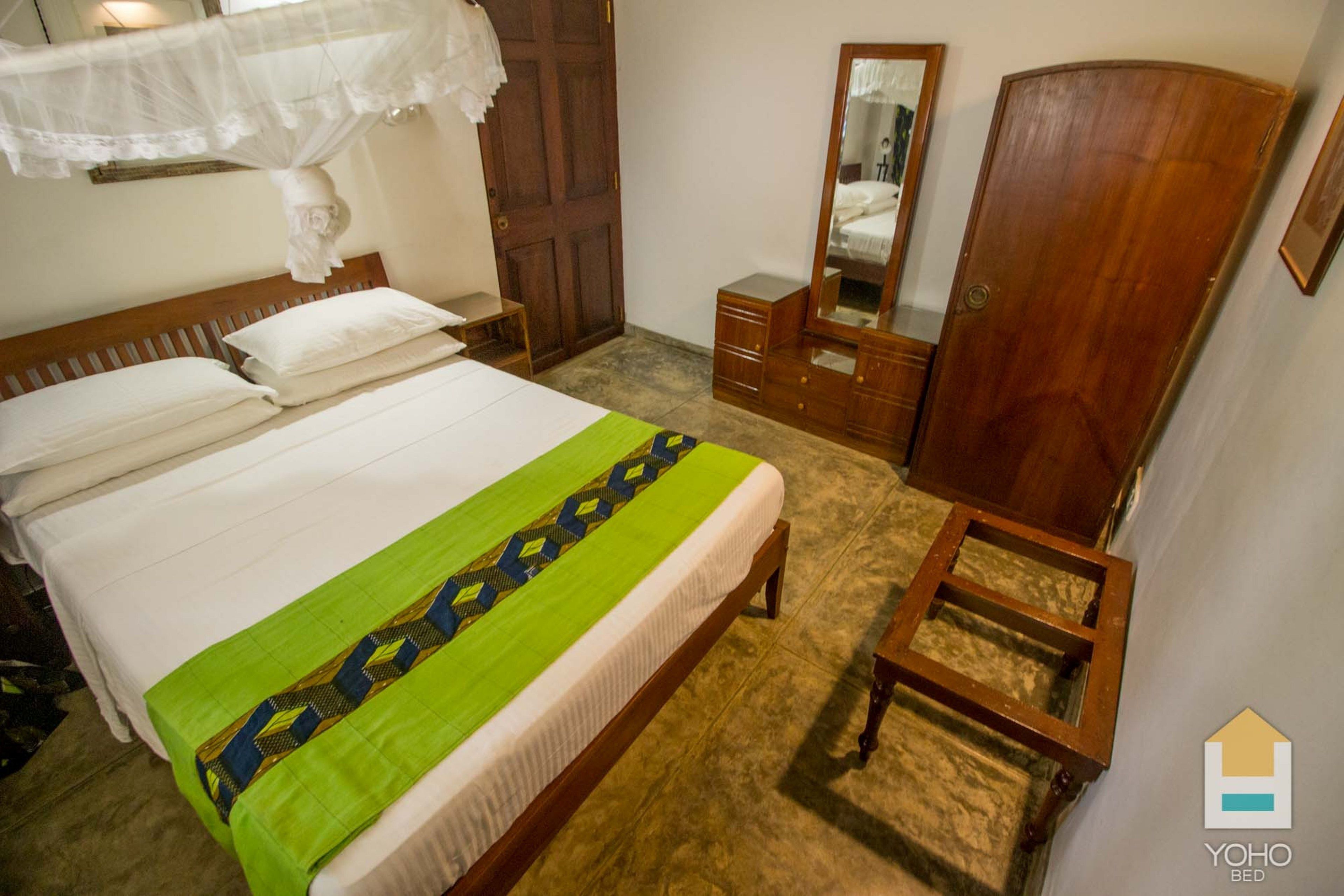 Quarto com cama, guarda-roupa de madeira, mesa de cabeceira e espelho.
