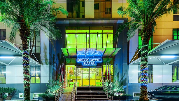 Entrada do Bravo Royal Hotel com design moderno, destacando uma placa e palmeiras.