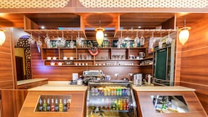 Uma área de bar com prateleiras de madeira, uma exposição de frutas e uma máquina de café.