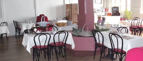 Um restaurante com várias mesas e cadeiras, toalhas de mesa brancas e luminárias pendentes.
