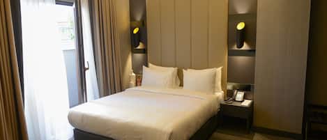 Quarto de hotel com uma cama grande, uma mesa de cabeceira com telefone e um criado-mudo com abajur.