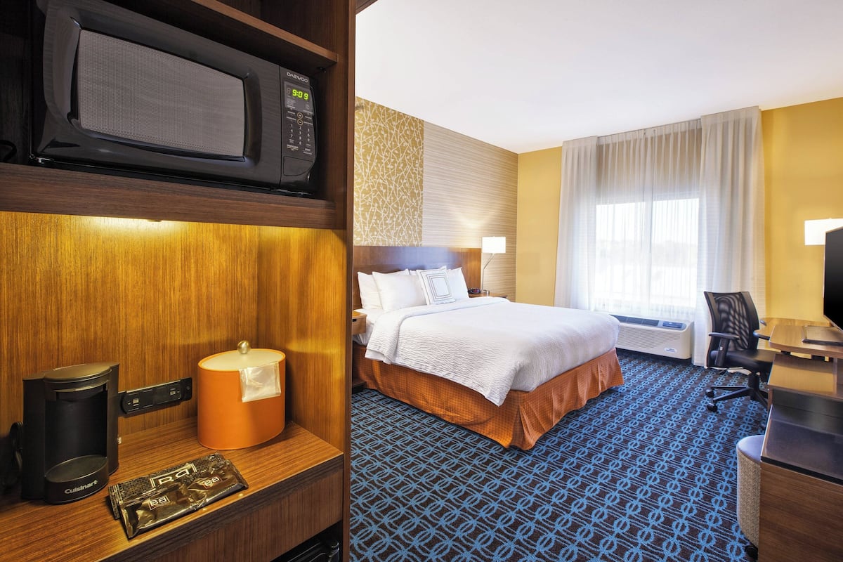 Quarto de hotel com cama, escrivaninha, micro-ondas, cafeteira e lixeira.
