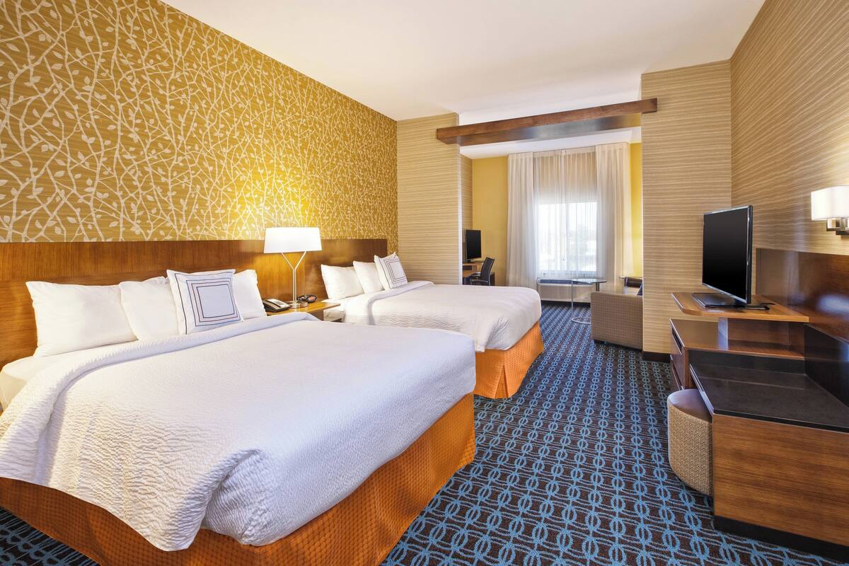 Quarto de hotel com duas camas, uma mesa, uma televisão e um banheiro.