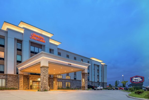 Hotel Hampton Inn & Suites com design moderno, apresentando entrada coberta e uma placa de endereço bem visível.
