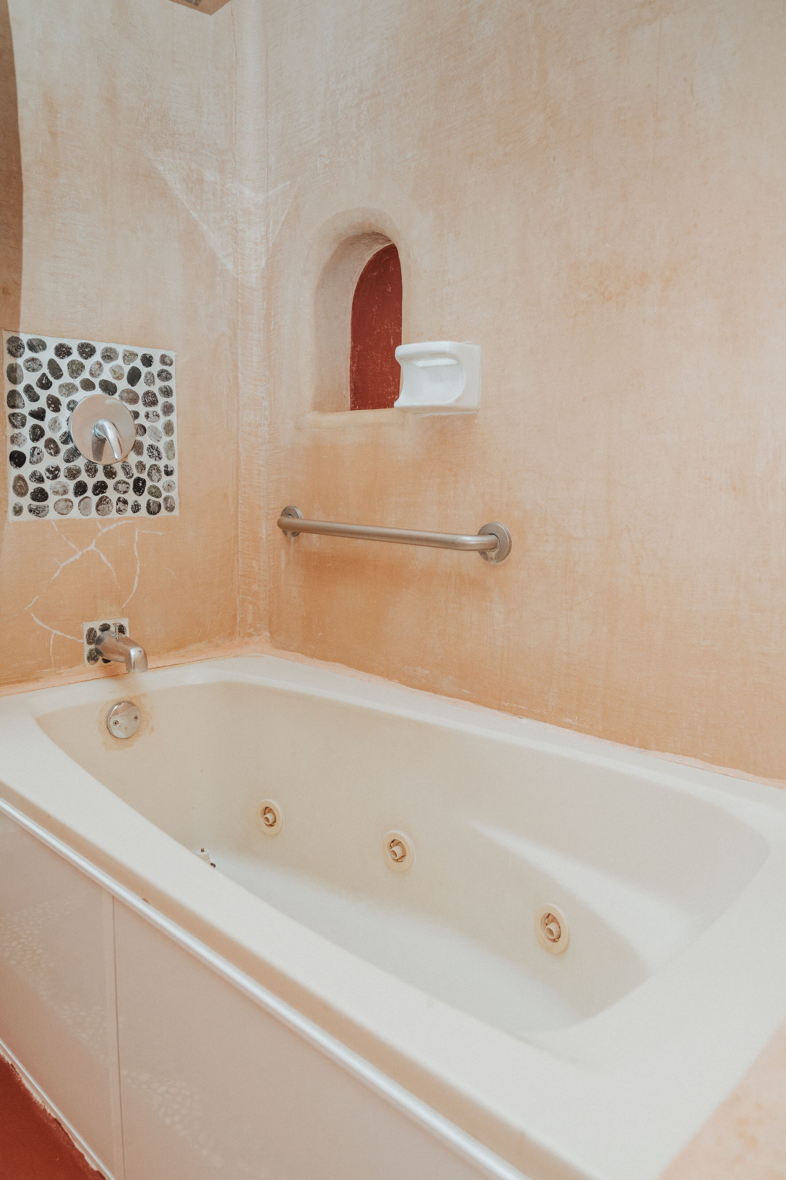 Uma banheira com barra de apoio, uma pequena prateleira com uma toalha e decoração em mosaico.