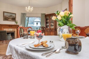 Mesa de jantar posta com itens de café da manhã, incluindo croissants, frutas e um jarro de suco de laranja.