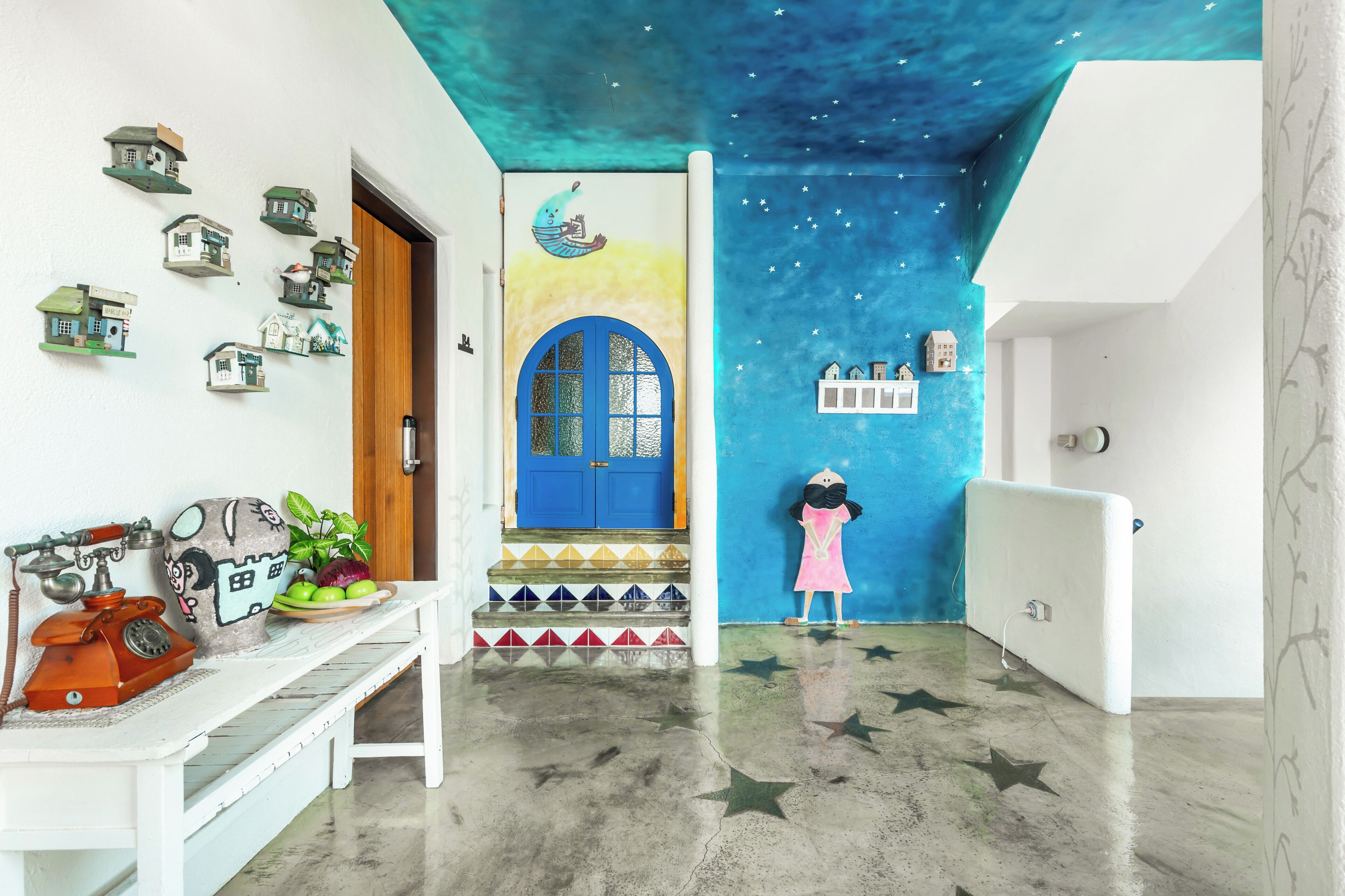 Um quarto com uma porta azul, um banco com telefone e uma parede com decorações de estrelas.