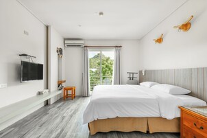 Quarto moderno com uma cama grande, televisão, mesa pequena e janela com cortinas.