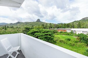 Uma varanda com uma cadeira branca, com vista para uma paisagem verdejante com colinas e edifícios ao fundo.