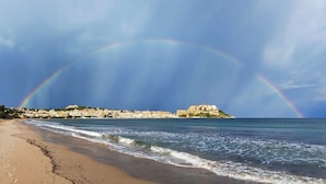 Uma praia com ondas, um arco-íris e um edifício numa colina.