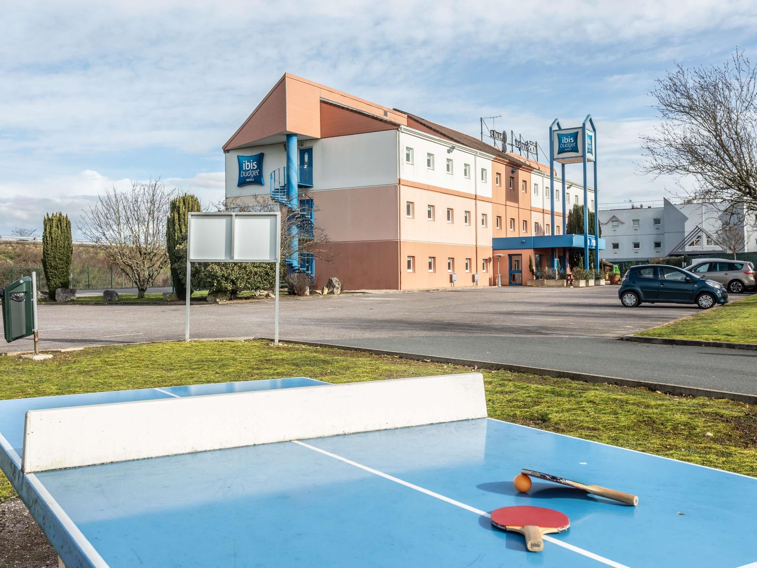 Um hotel com fachada azul e branca, quadra de tênis e estacionamento.