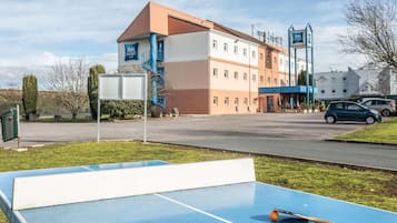 Um hotel com fachada azul e branca, quadra de tênis e estacionamento.