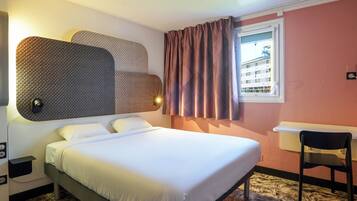 Quarto de hotel com cama, escrivaninha e cadeira.