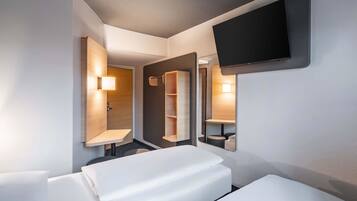 Quarto de hotel moderno com uma cama, uma televisão fixada na parede e um espelho refletindo o ambiente.