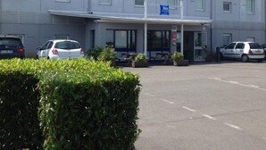 Um edifício com a placa 'ibis budget', indicando ser um hotel econômico. Há carros estacionados em frente e um céu claro acima.