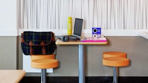 Uma pequena mesa com um laptop, fones de ouvido, uma garrafa de água, um livro e uma bolsa.